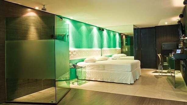 Quarto moderno com divisória de vidro, cama com roupa de cama branca e escrivaninha com cadeira.