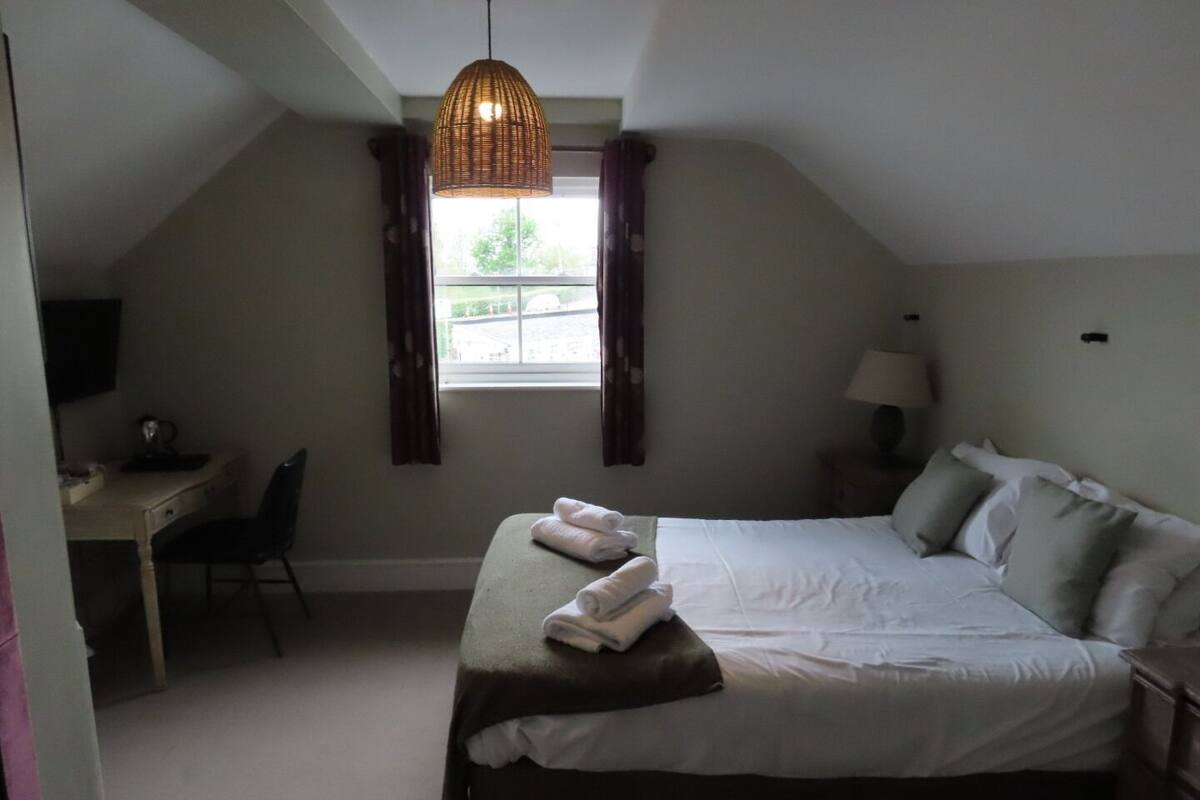 Quarto com cama, escrivaninha, cadeira, luminária e janela com cortinas.