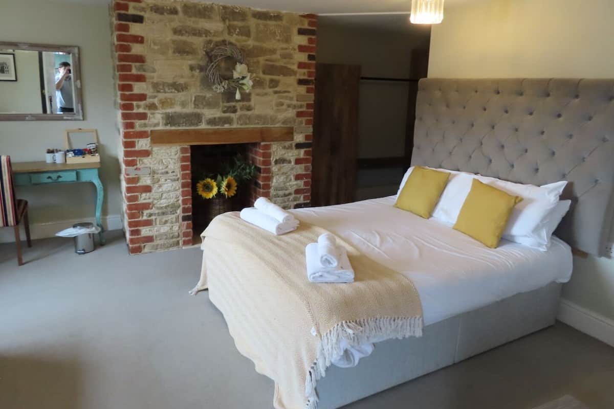 Um quarto com uma cama grande, uma lareira de tijolos e uma escrivaninha com uma cadeira.