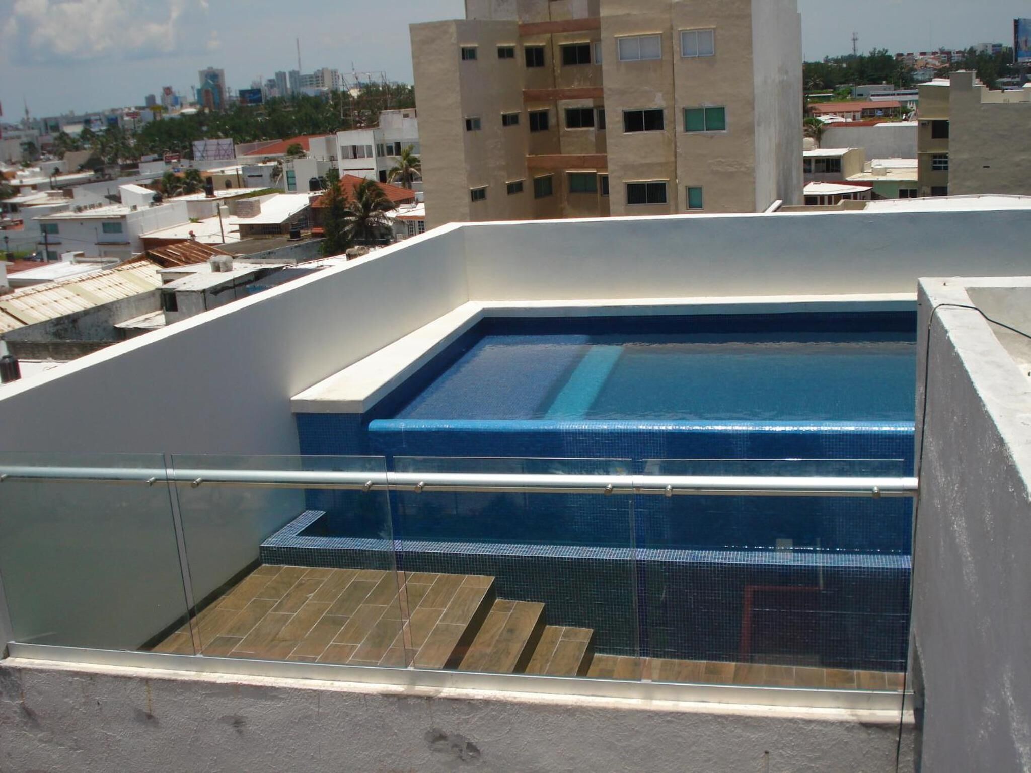 Piscina no terraço com guarda-corpo de vidro, cercada por edifícios urbanos.