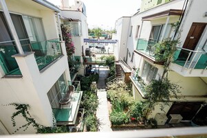 Um pátio urbano estreito com várias varandas, uma escadaria central e uma pequena área ajardinada.