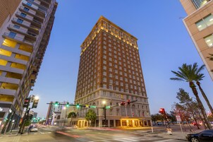Um hotel de vários andares com arquitetura clássica, situado num cruzamento movimentado com semáforos e placas de rua.