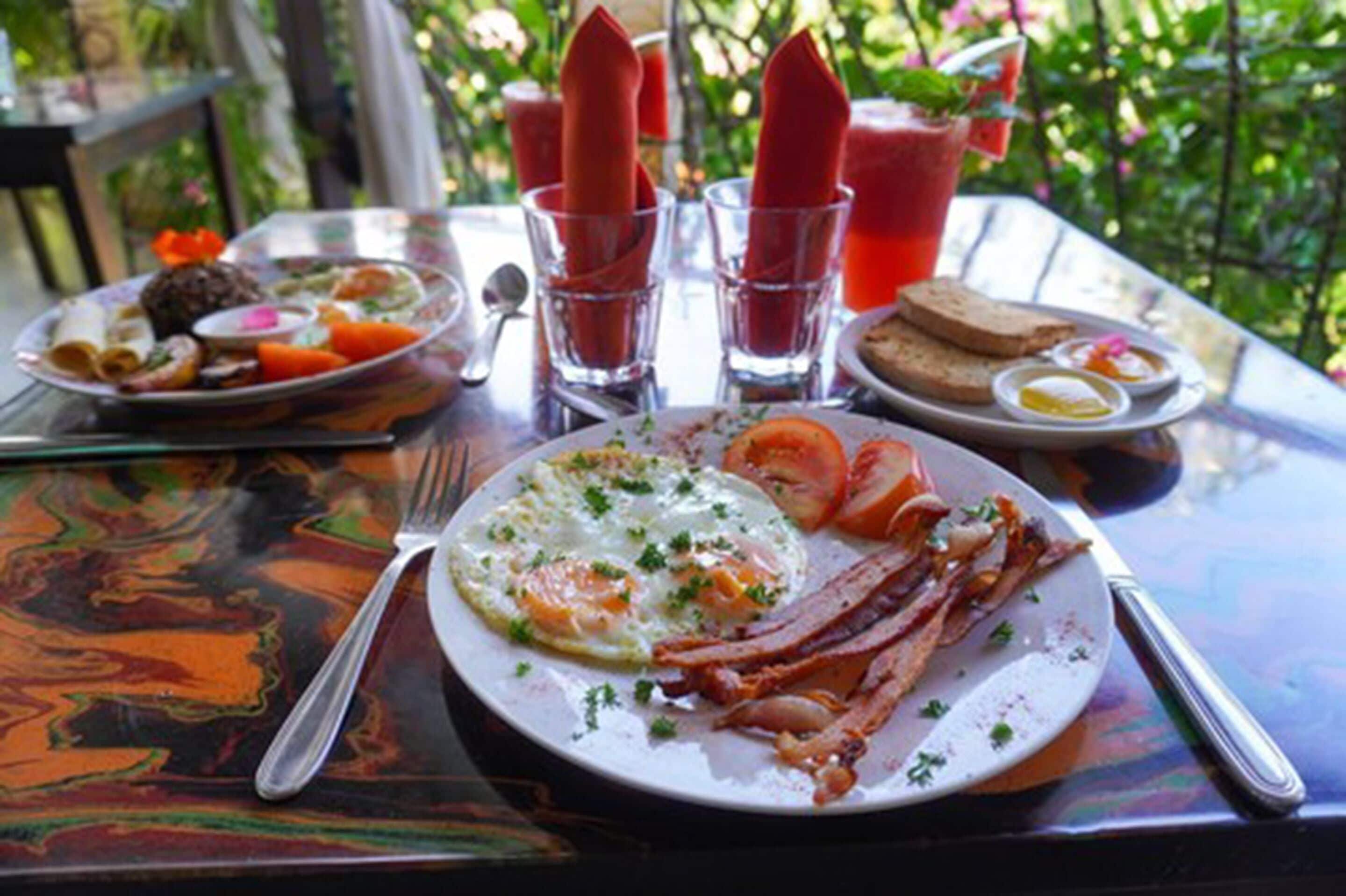 Uma mesa de café da manhã com pratos de comida, copos de suco e um garfo.