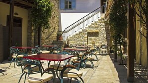 Um café ao ar livre com paredes de pedra e uma escadaria que leva a um andar superior.