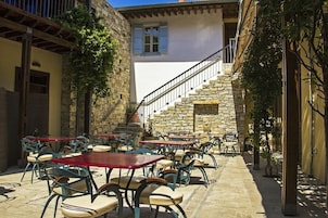 Um café ao ar livre com paredes de pedra e uma escadaria que leva a um andar superior.