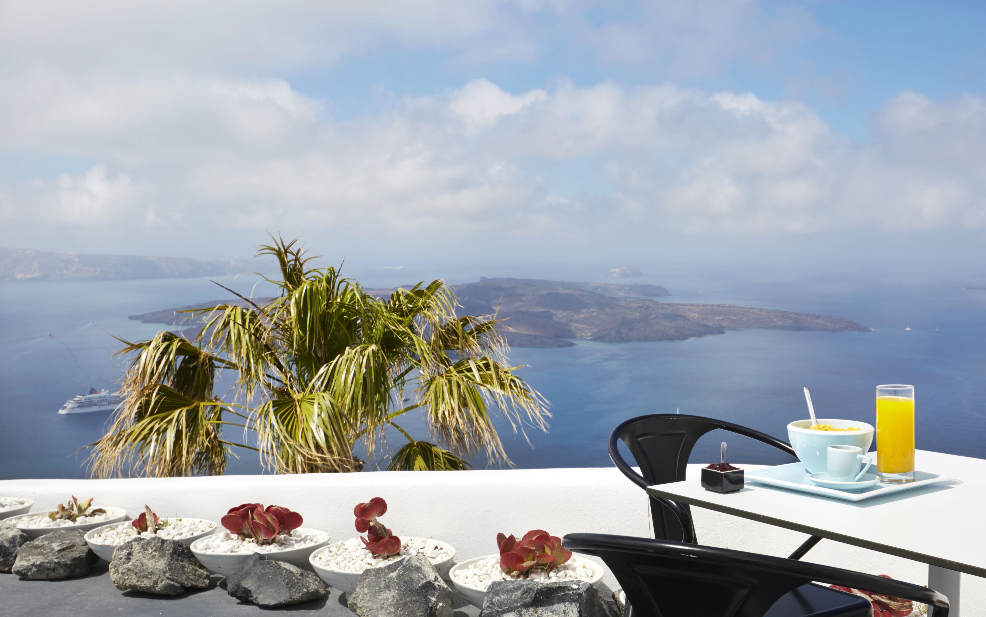 Mesa com copo de suco de laranja, xícara e tigela de comida, com vista panorâmica do mar e ilhas.
