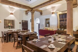 Uma ampla área de refeições com várias mesas e cadeiras de madeira, um buffet central e um teto alto com vigas aparentes.
