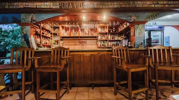 Uma área de bar com cadeiras de madeira, prateleiras cheias de garrafas e uma placa acima com a inscrição 'PURA VIDA'.