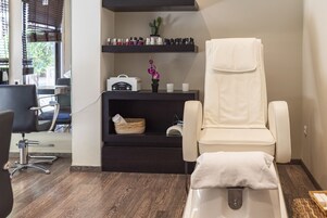 Uma cadeira de massagem, uma estante com diversos objetos e uma cadeira num quarto com soalho de madeira.