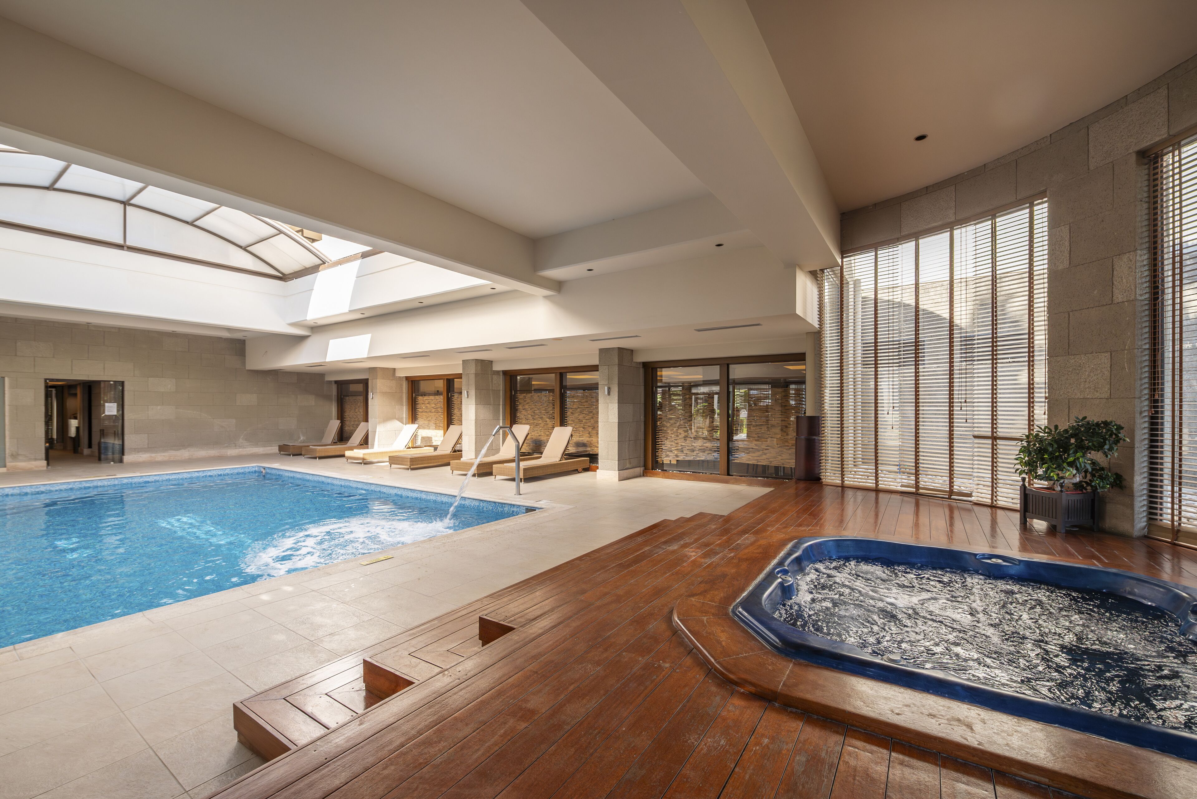 Piscina interior ampla com hidromassagem, espreguiçadeiras e claraboia.