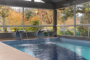 Piscina com duas fontes e amplas janelas com vista para um jardim com folhagem de outono.