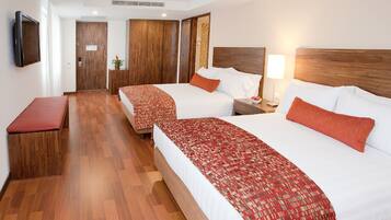 Quarto de hotel com duas camas, um banco, uma TV e uma porta para um banheiro.