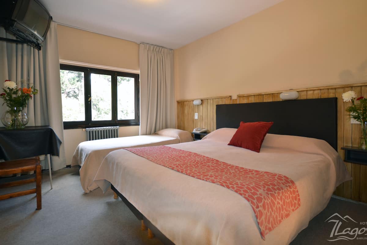 Quarto de hotel com duas camas, uma escrivaninha com cadeira, uma janela com cortinas e um radiador.