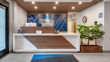 Uma receção de hotel com design moderno, incluindo um painel de parede azul geométrico, um balcão de madeira e uma planta em vaso.