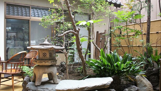 Um jardim japonês tradicional com um lampião de pedra, cadeiras de madeira e uma cerca de bambu.