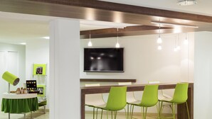 Uma área de bar moderna com televisão de tela plana, banquetas verdes e uma mesa coberta por toalha verde.