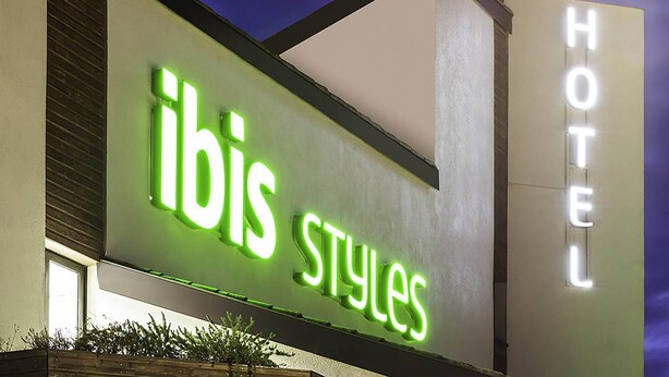 Placa de hotel com 'ibis styles' iluminado em luzes de neon verdes.