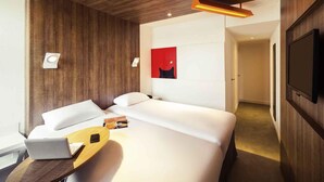 Quarto de hotel moderno com teto de madeira, cama com roupa de cama branca, escrivaninha com um laptop e televisão na parede.