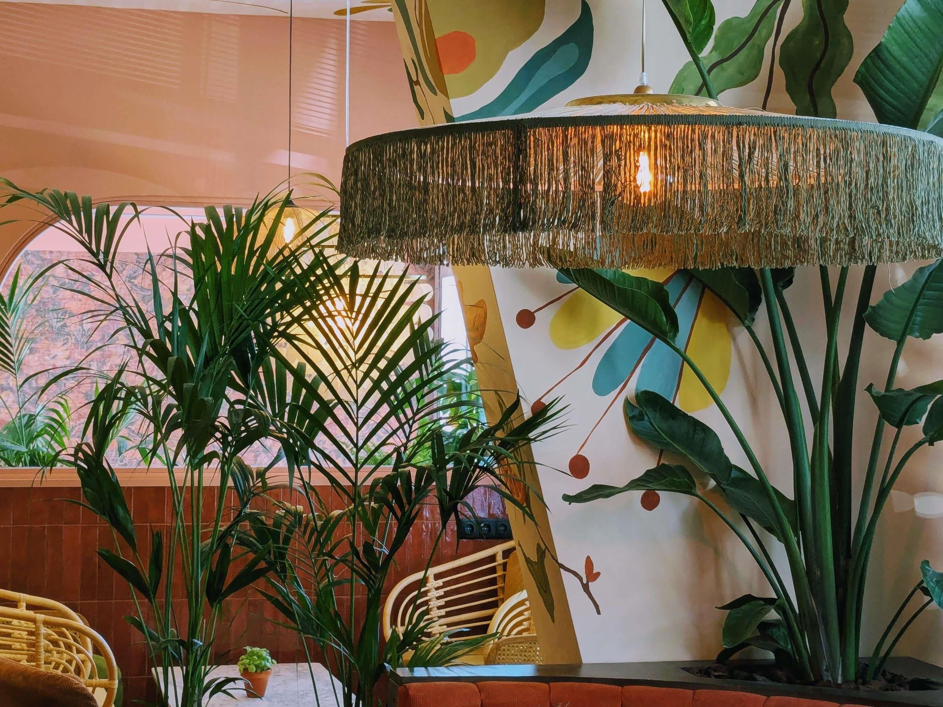 Um quarto com uma luminária pendente grande, uma cadeira de vime e diversos vasos com plantas.
