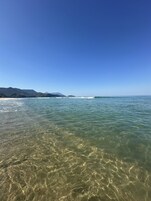 Vista clara de uma praia com ondas suaves e uma cordilheira ao longe.