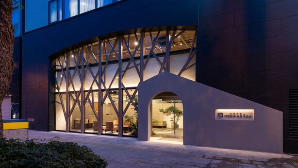 Uma entrada de hotel moderna com fachada de vidro em arco e área de estar interna visível.