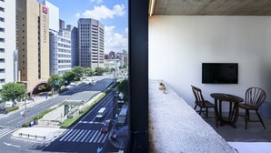 Uma varanda com vista para uma rua da cidade, uma mesa com cadeiras e uma televisão montada.