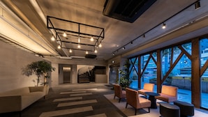 Um hall espaçoso com design moderno, destacando uma escadaria central, área de estar com sofás e mesas, e grandes janelas com vista para o exterior.