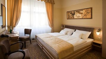 Quarto de hotel com uma cama grande, uma escrivaninha com cadeira, um telefone e um candeeiro fixado na parede.
