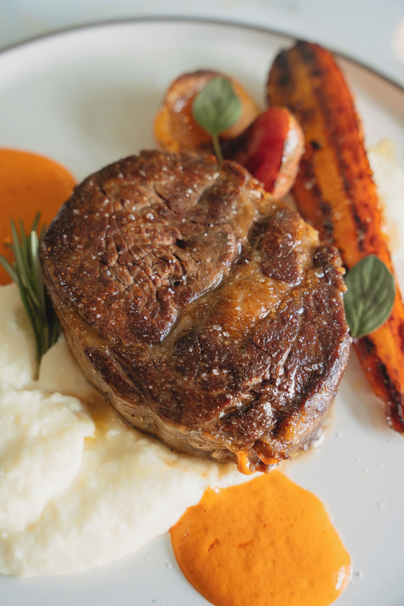 Bife com purê de batata e legumes grelhados em um prato.