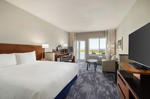 Quarto de hotel com uma cama grande, uma escrivaninha com computador, uma TV, uma cadeira e vista para o exterior.
