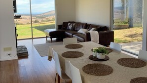Ampla sala de estar com uma grande mesa de jantar, sofá de couro e vista para o campo.
