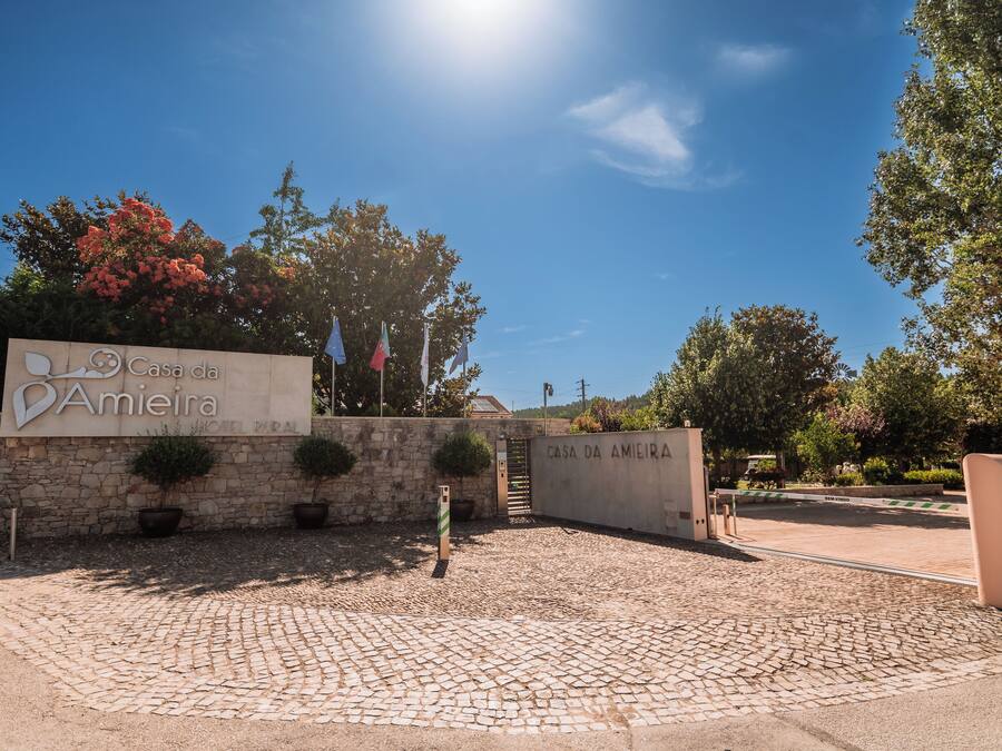 Entrada de hotel com caminho de paralelepípedos, muro de pedra e placa com o nome Casa da Amieira.