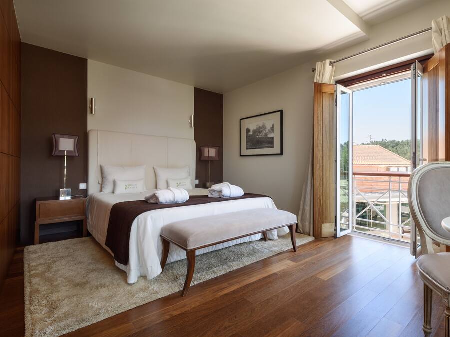 Quarto de hotel com cama, mesas de cabeceira, um banco, uma cadeira e vista para o exterior.