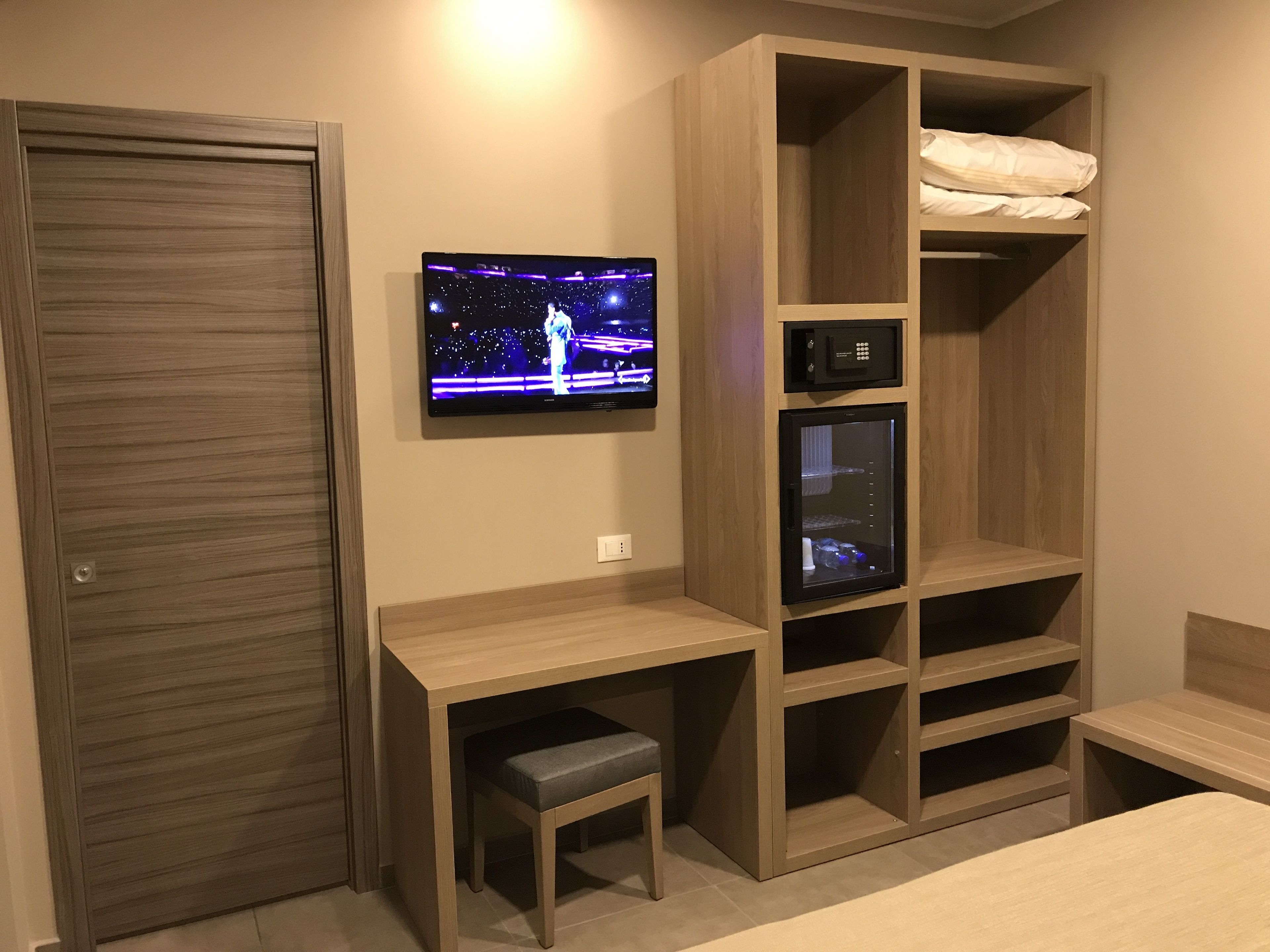 Quarto com escrivaninha de madeira, televisão, guarda-roupa e cama.