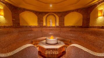 Um espaço de spa com uma bacia de pedra central, área de estar e uma estátua ao fundo.