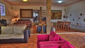 Uma sala espaçosa com um sofá grande, uma poltrona menor, uma mesa de centro e uma mesa de jantar posta para quatro pessoas.