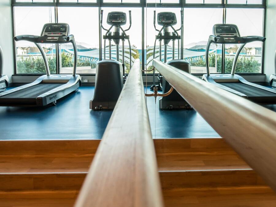 Uma academia com esteiras e aparelhos elípticos, amplas janelas e piso de madeira.