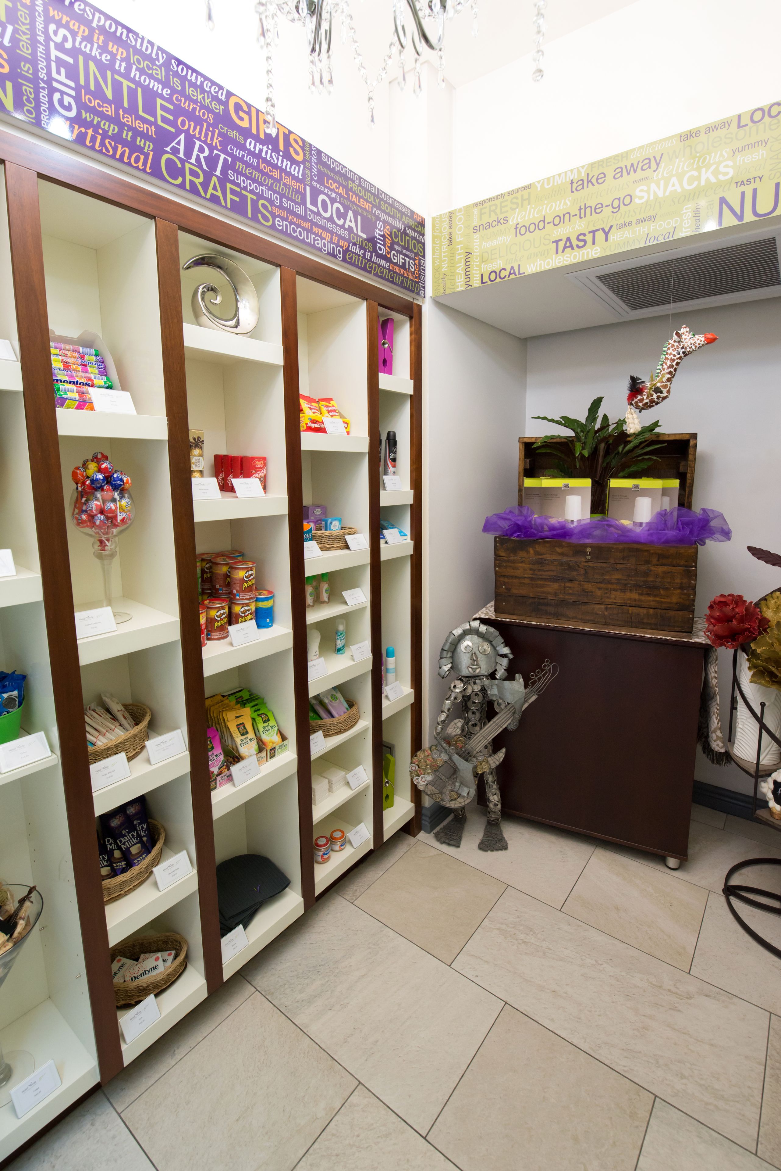 Uma loja de artesanato com prateleiras repletas de diversos produtos, uma vitrine de madeira com uma planta e uma escultura de metal decorativa.