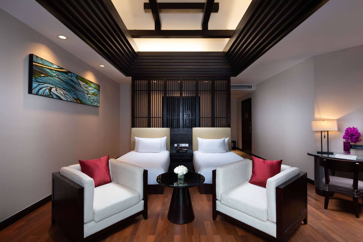 Quarto de hotel moderno com dois sofás brancos, uma mesa de centro preta e uma grande pintura abstrata na parede.