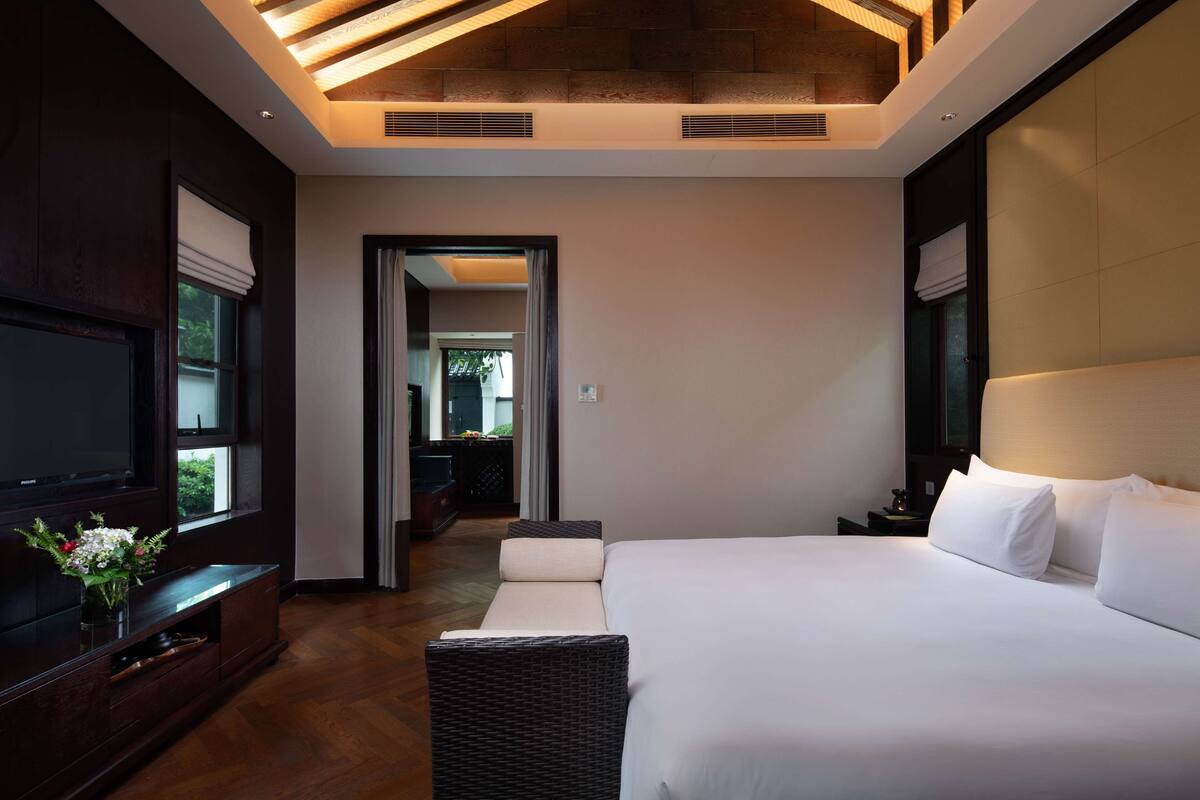 Quarto de hotel moderno com uma cama grande, uma televisão e um design de teto em madeira.