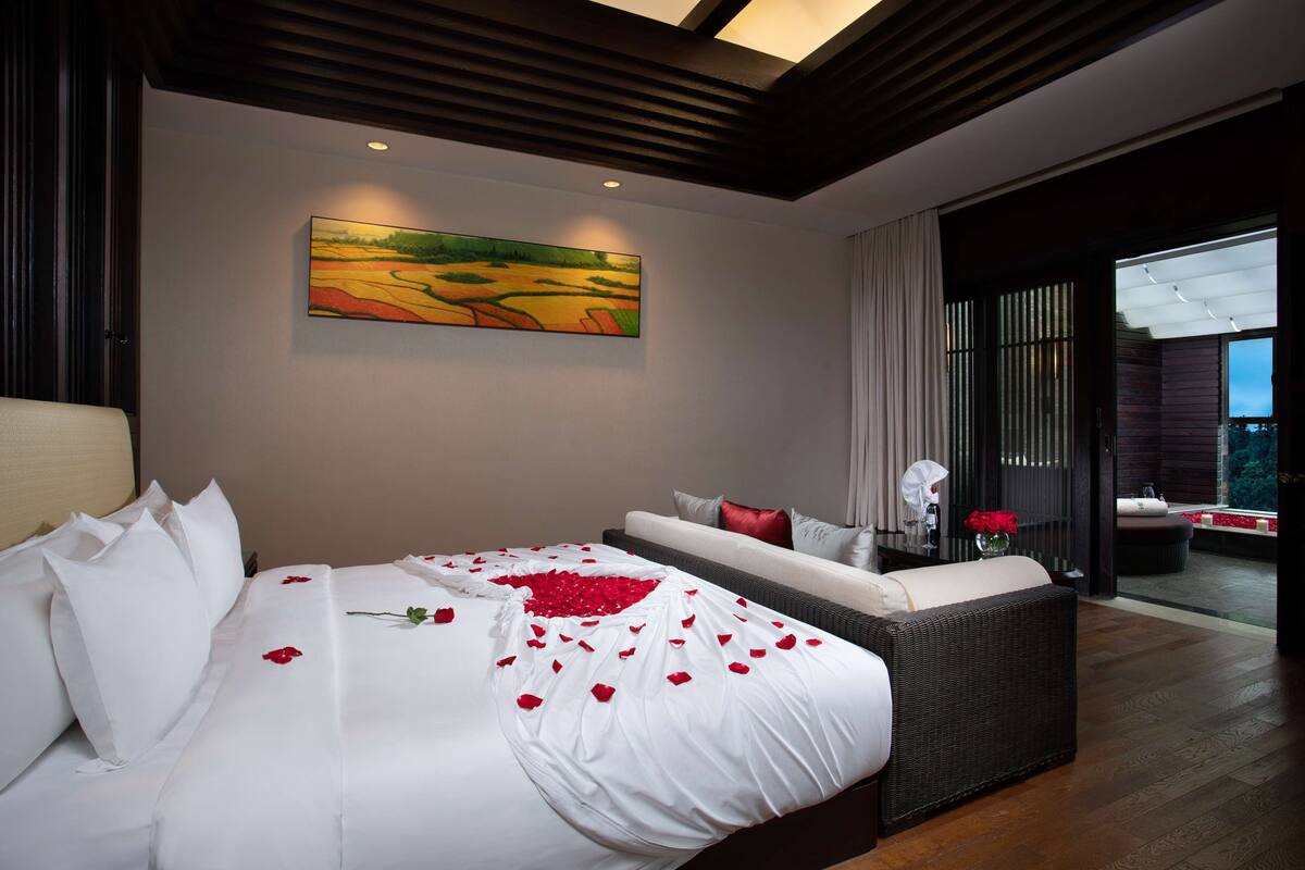 Quarto de hotel com cama, sofá, um quadro na parede e vista através de uma porta de vidro.