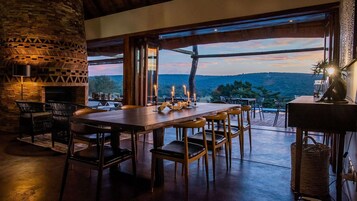 Uma sala de jantar com lareira de pedra, mesas e cadeiras de madeira, com vista para uma paisagem deslumbrante.