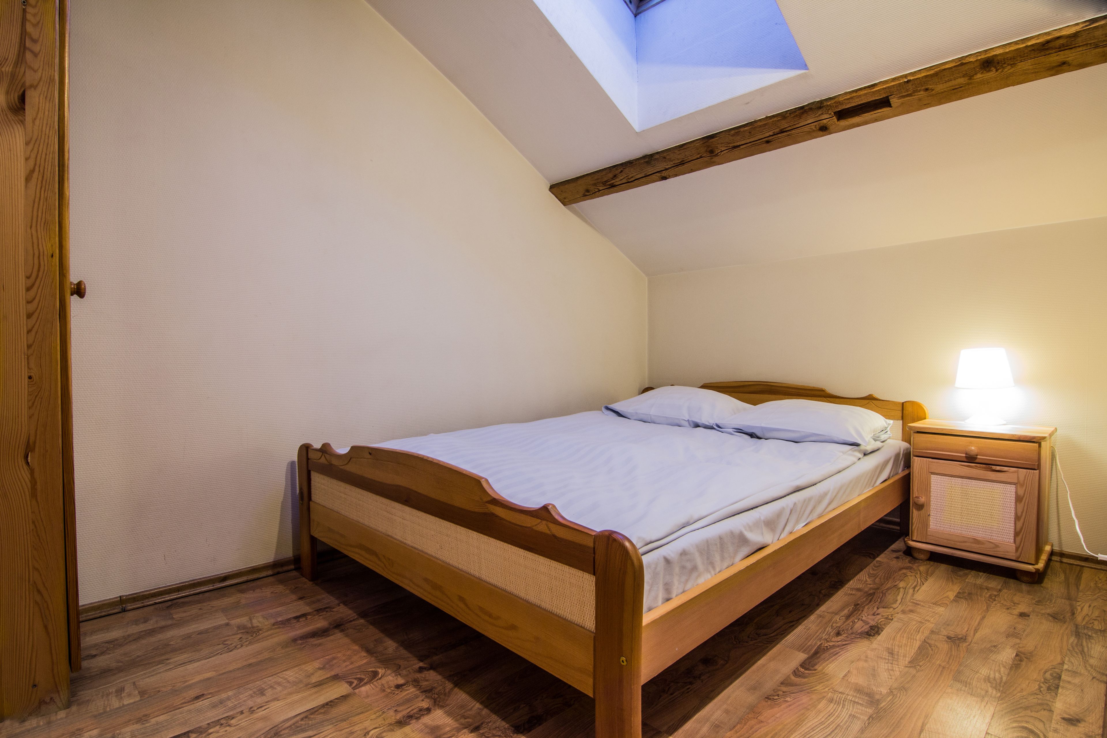 Quarto com cama de madeira, mesa de cabeceira e claraboia.