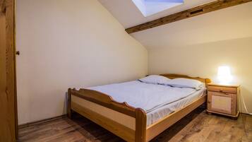 Quarto com cama de madeira, mesa de cabeceira e claraboia.