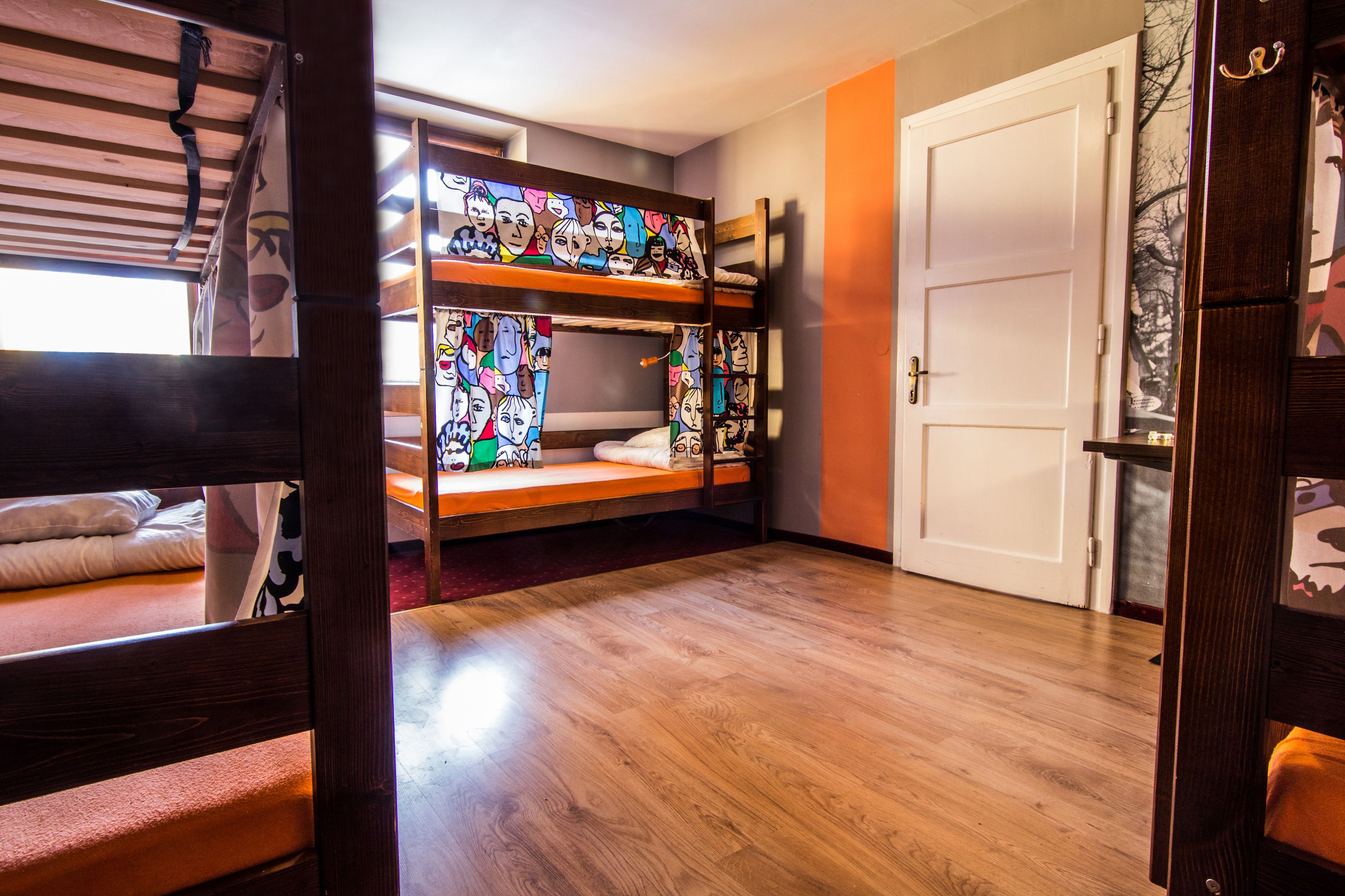 Quarto com beliche, piso de madeira, porta branca e parede com mural.