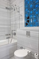 Casa de banho com chuveiro, sanita e parede decorativa com azulejos azuis.