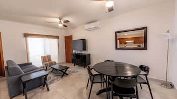 Uma sala de estar moderna com sofá, mesa de centro, mesa de jantar com cadeiras, televisão e ventiladores de teto.