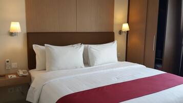 Quarto de hotel com uma cama grande, duas luminárias de cabeceira, um painel de cabeceira de madeira e um detalhe vermelho no cobreleite.