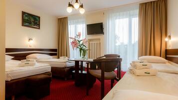 Quarto de hotel com duas camas, uma mesa de jantar, uma cadeira, um vaso com flores, um quadro na parede e uma televisão.