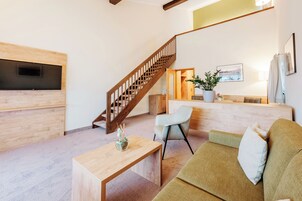Uma sala de estar moderna com escada de madeira, televisão de tela plana presa a um painel de madeira, sofá, mesa de centro e um vaso com planta.